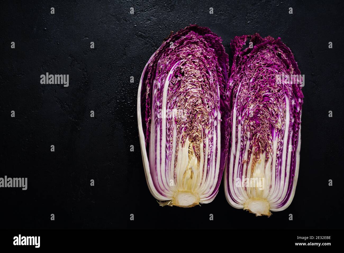 Fresh raw purple Chinese cabbage cut in half on a black concrete old ...