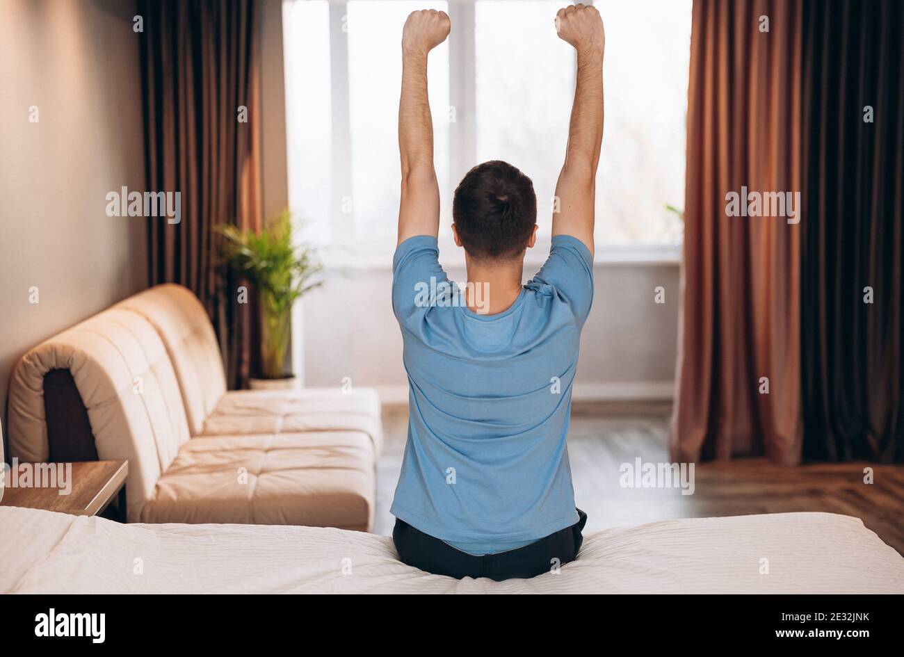Good morning Young man waking up in bed and stretching his arms, back ...