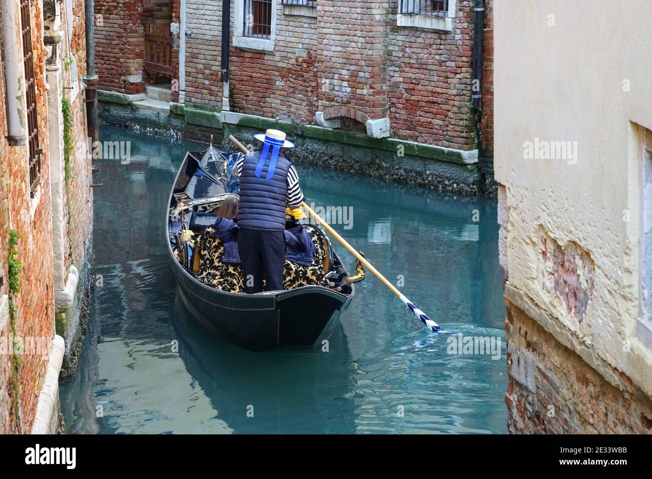 Gondolier on traditional Venetian gondola with tourists on canal in ...