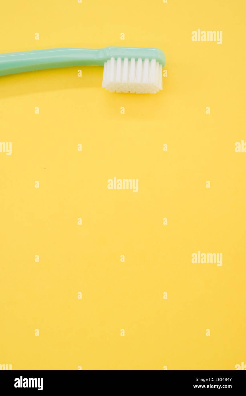 Vertical shot of turquoise toothbrush on a yellow surface for a copy ...