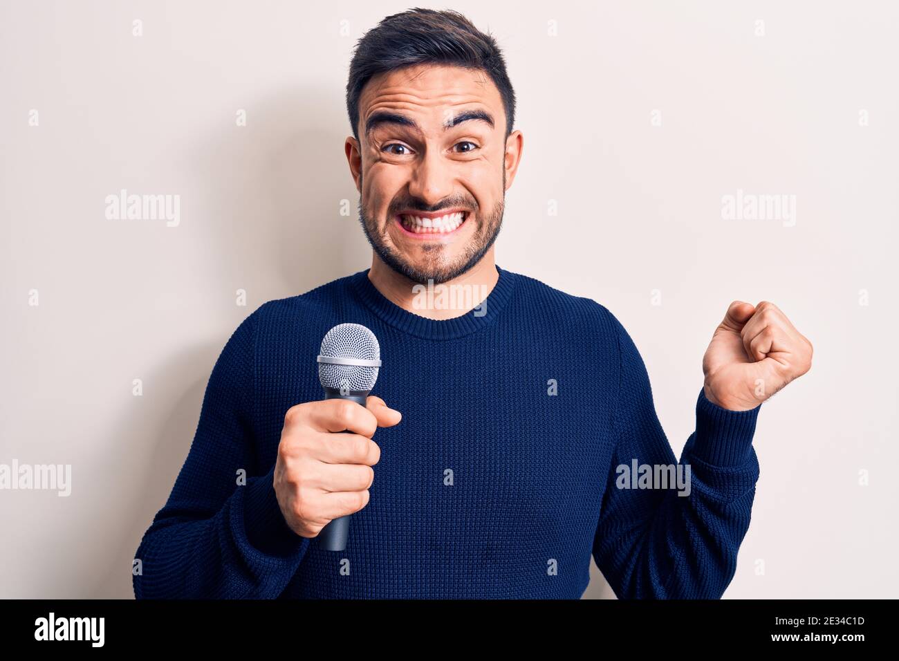 Young handsome singer man with beard singing song using microphone over white background ...