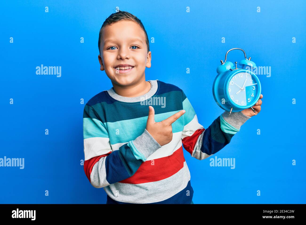 Little kid boy holding alarm clock smiling happy pointing with hand and ...