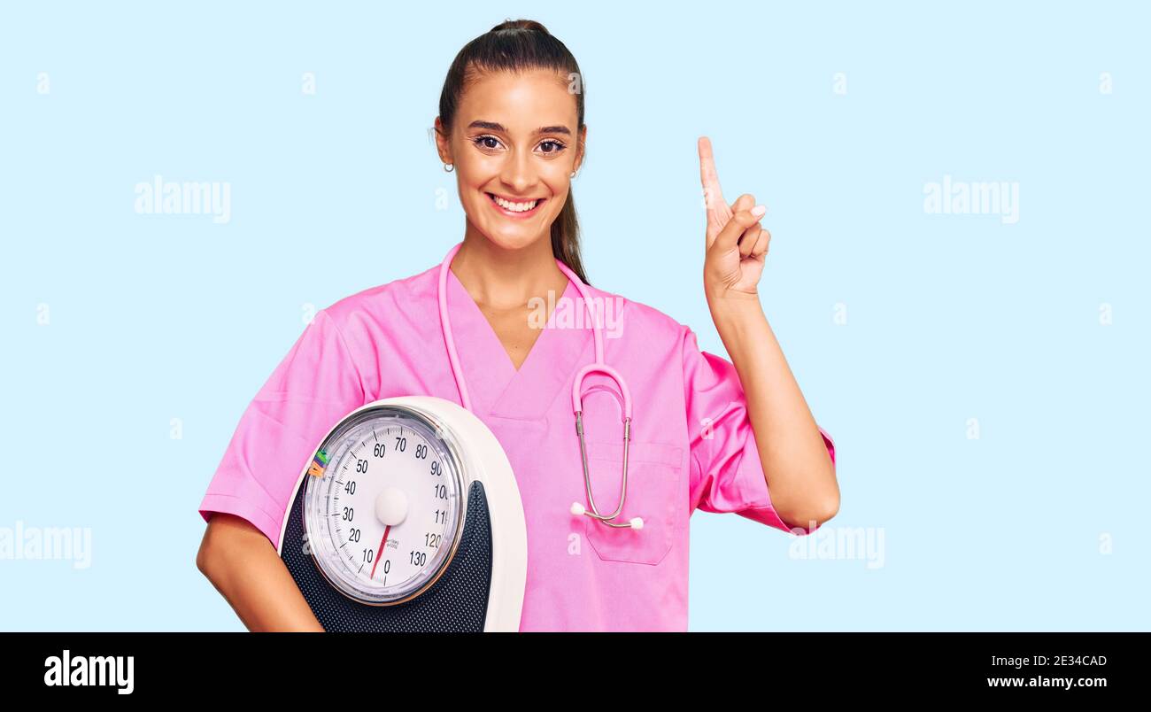 Young hispanic woman as nutritionist doctor holding weighing machine ...