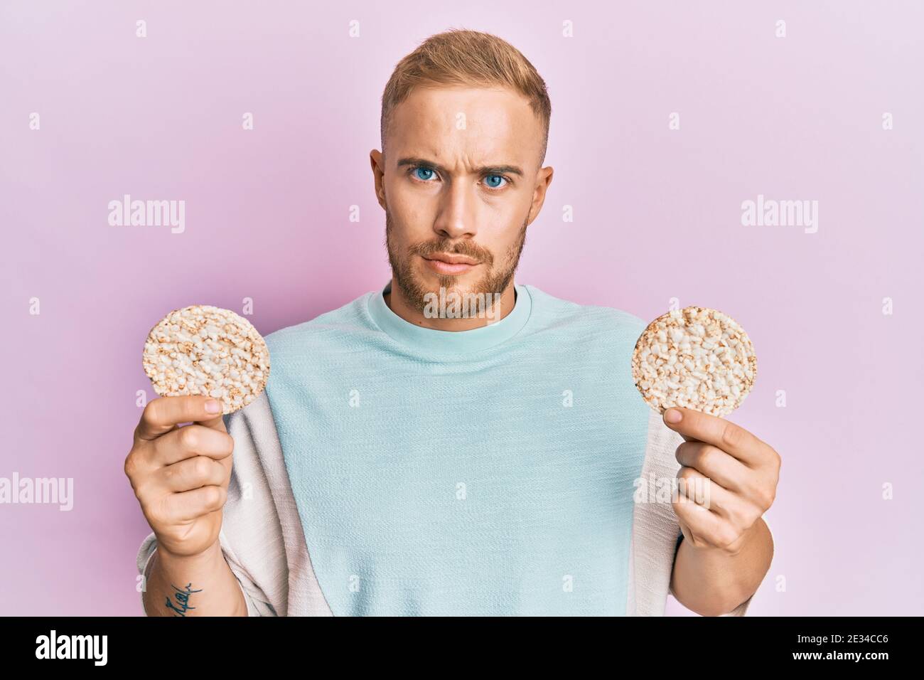 Young caucasian man eating healthy rice crackers skeptic and nervous ...