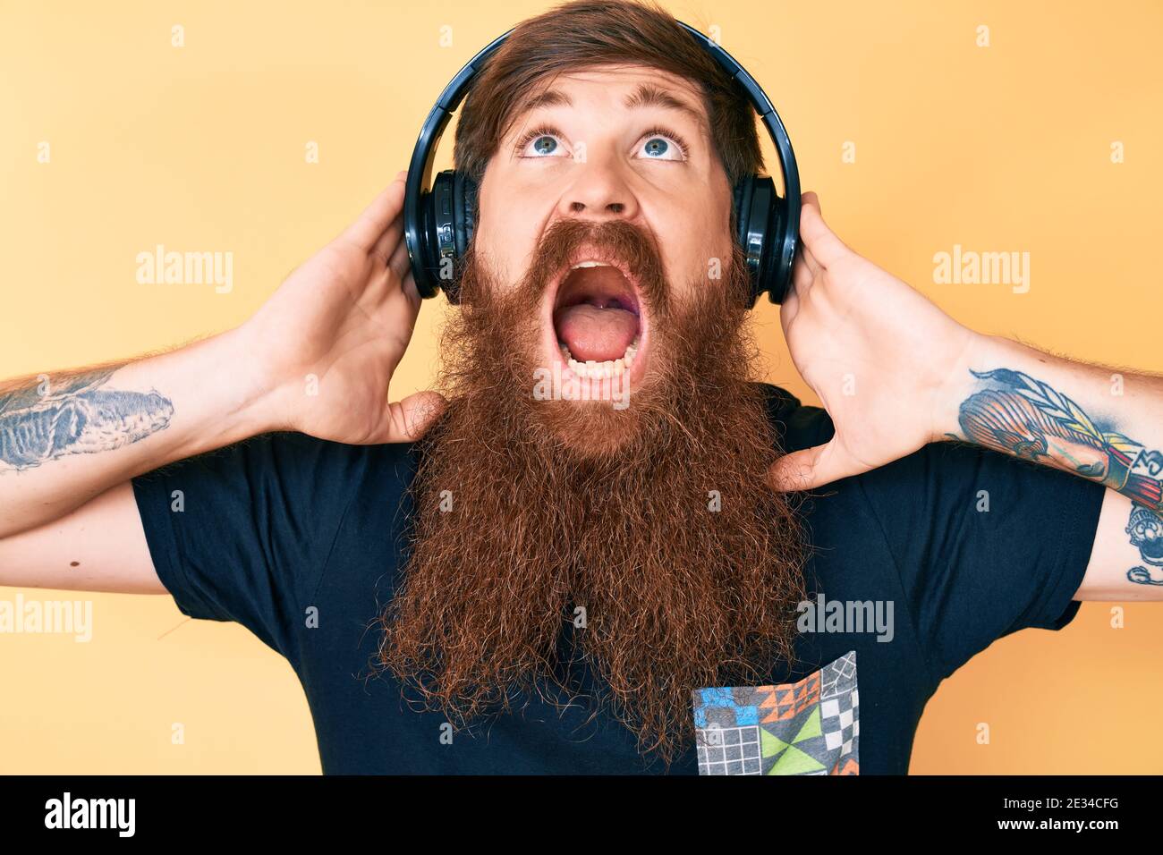 Handsome young red head man with long beard listening to music using ...