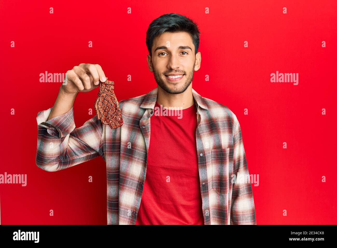Young handsome man holding beef steak looking positive and happy ...