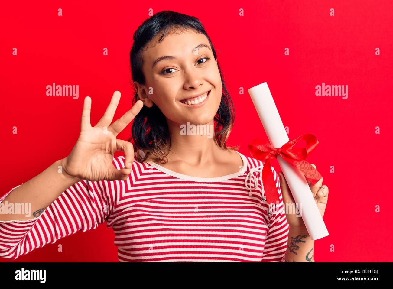 Young woman holding graduate degree diploma doing ok sign with fingers ... Young woman holding graduate degree diploma doing ok sign with fingers ...