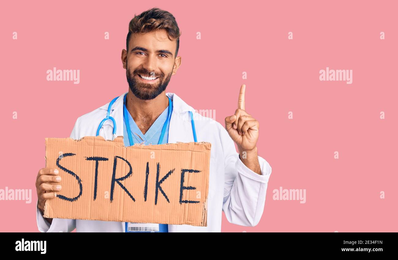 Young hispanic man wearing doctor stethoscope holding strike banner ...