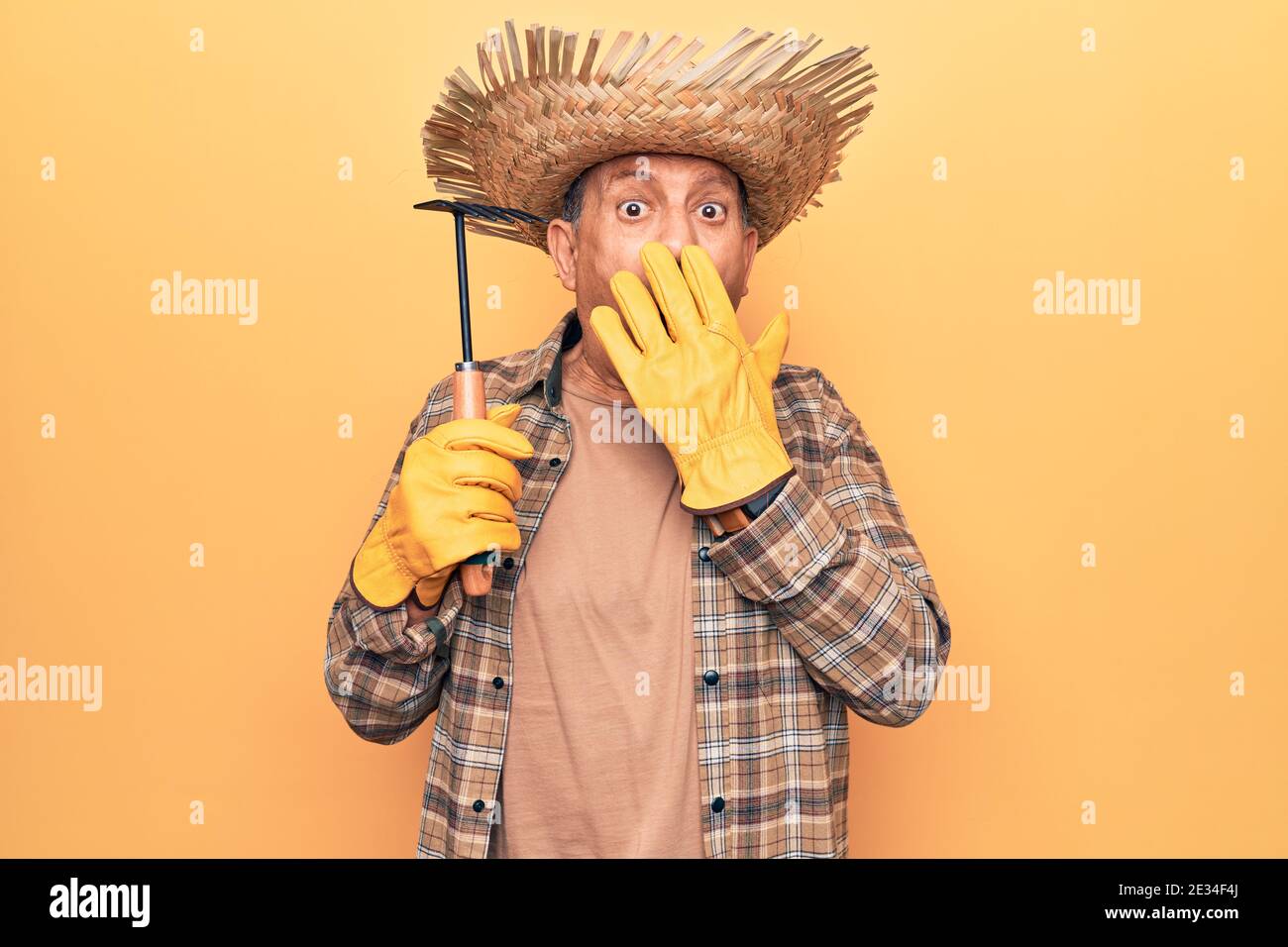 Senior man with grey hair wearing gardener hat holding rake covering ...