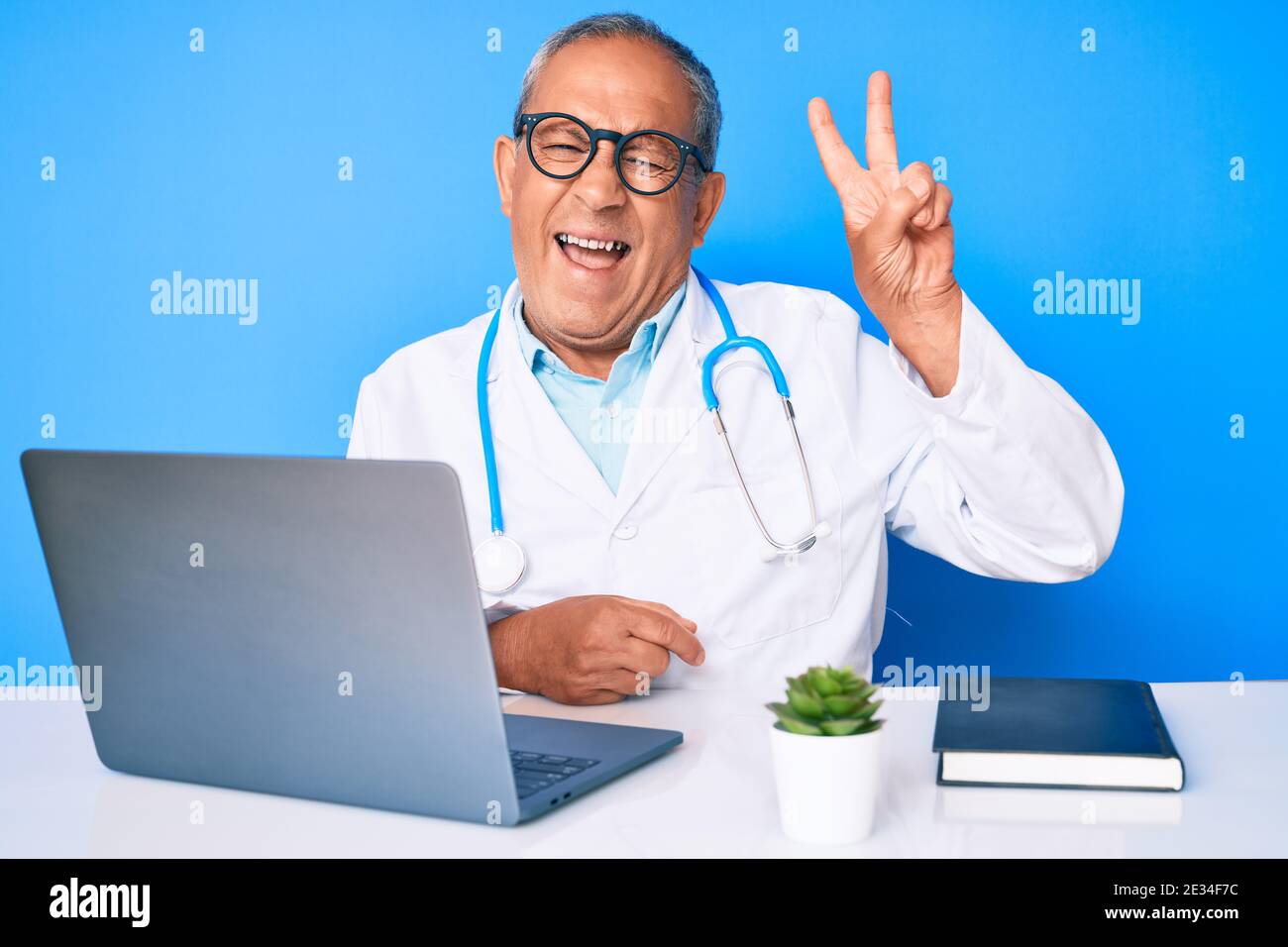 Senior handsome man with gray hair wearing doctor uniform working using ...