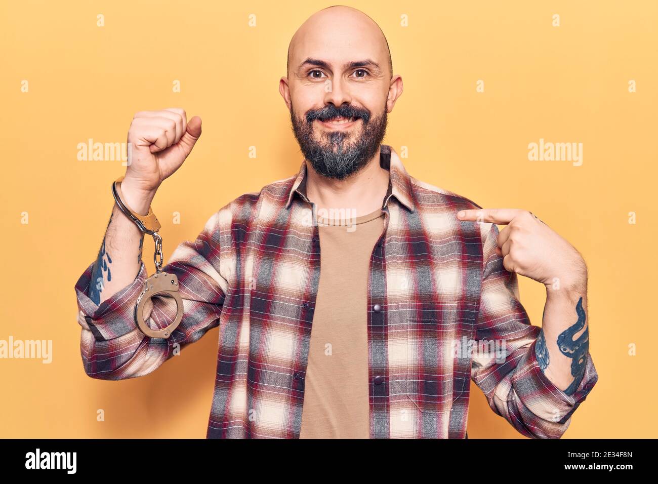 Young handsome man wearing prisoner handcuffs pointing finger to one ...
