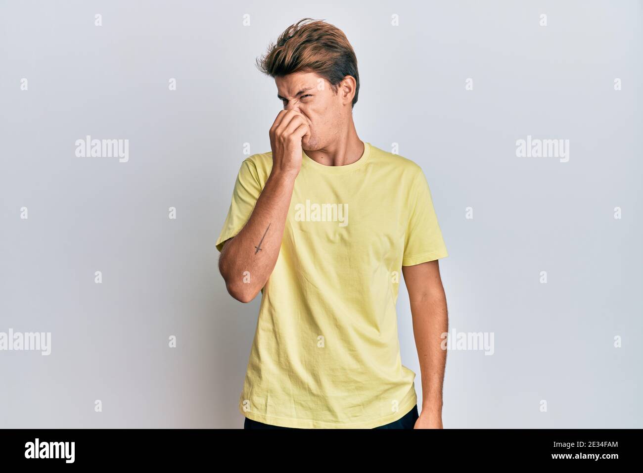 Handsome caucasian man wearing casual clothes smelling something stinky ...