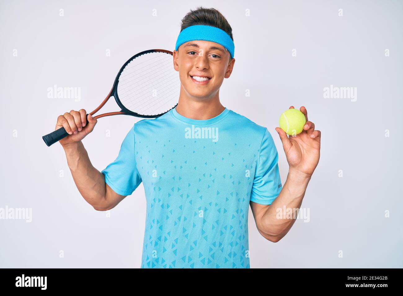 Young hispanic boy playing tennis holding racket and ball smiling with ...