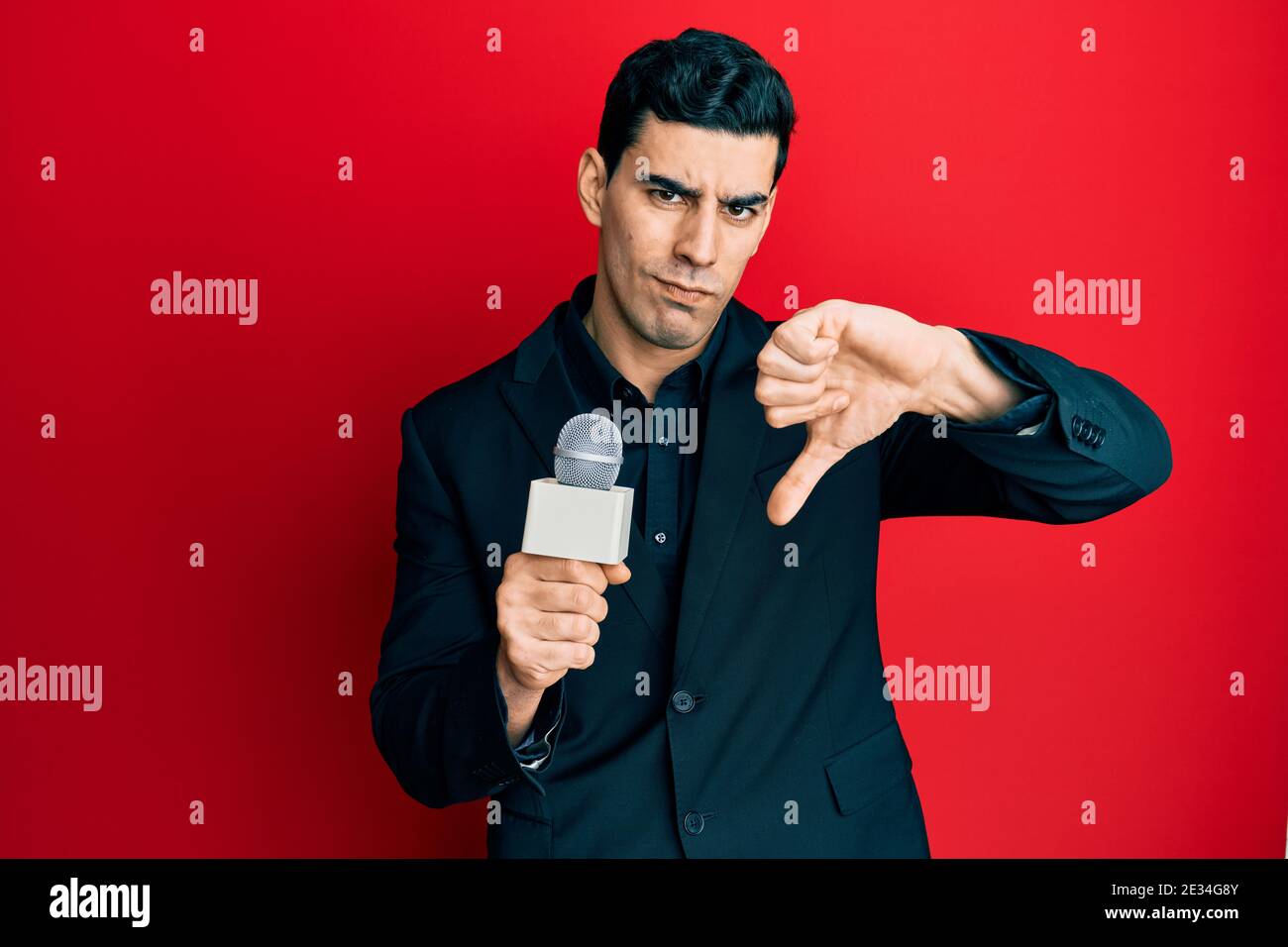 Handsome hispanic man holding reporter microphone with angry face ...