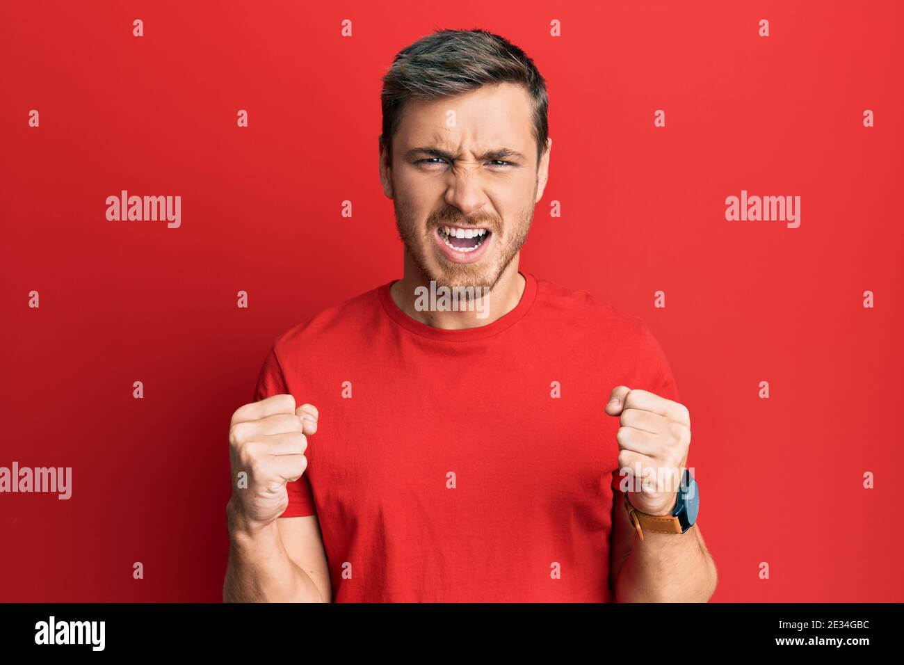 Handsome caucasian man wearing casual red tshirt angry and mad raising ...