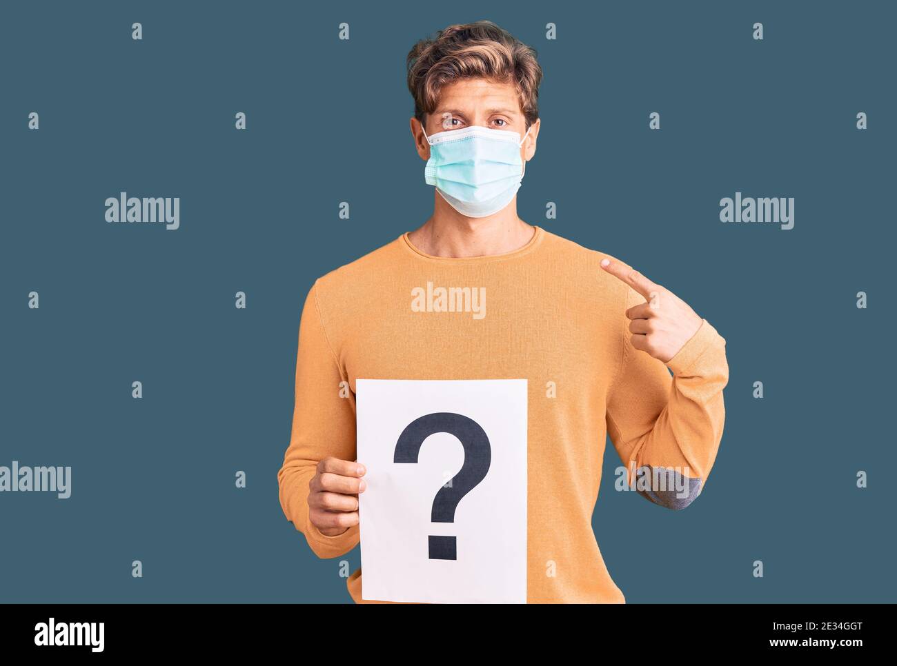 Young handsome man wearing medical mask holding question mark pointing ...