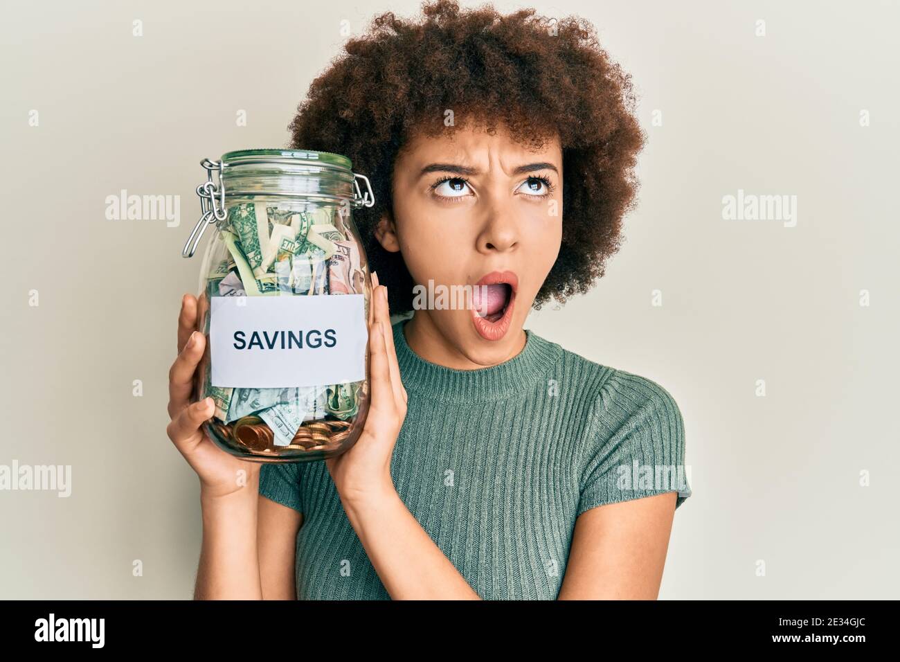 Young hispanic girl holding jar with savings angry and mad screaming ...