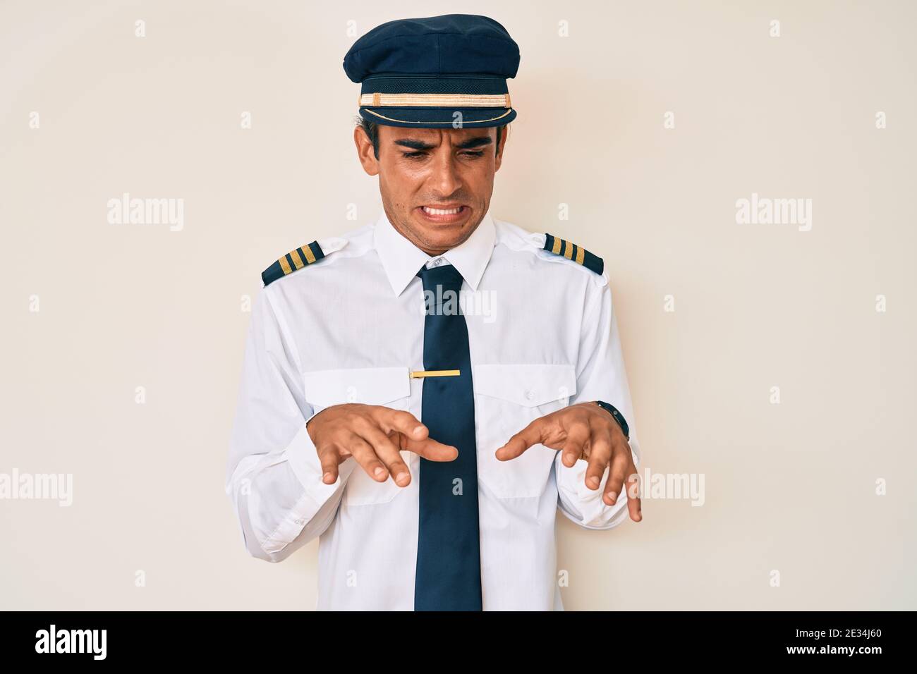 Young hispanic man wearing airplane pilot uniform disgusted expression ...