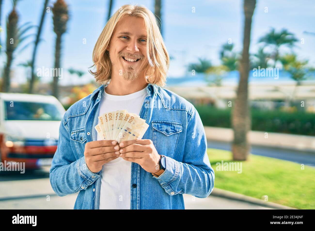 Young blond scandinavian man smiling happy holding danmark 100 kroner ...