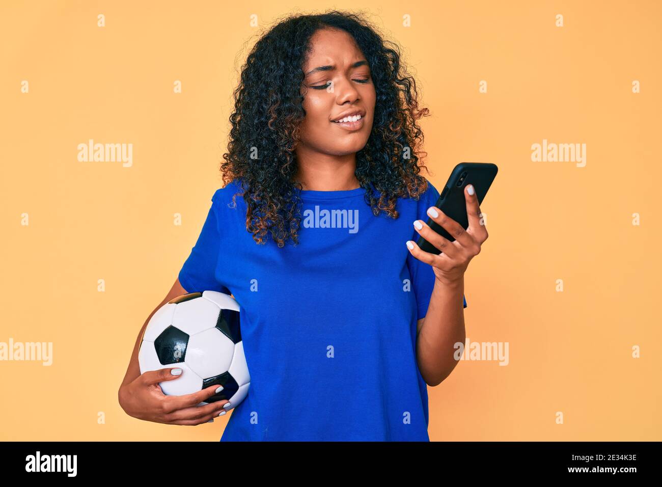 Young african american woman holding football ball looking at ...