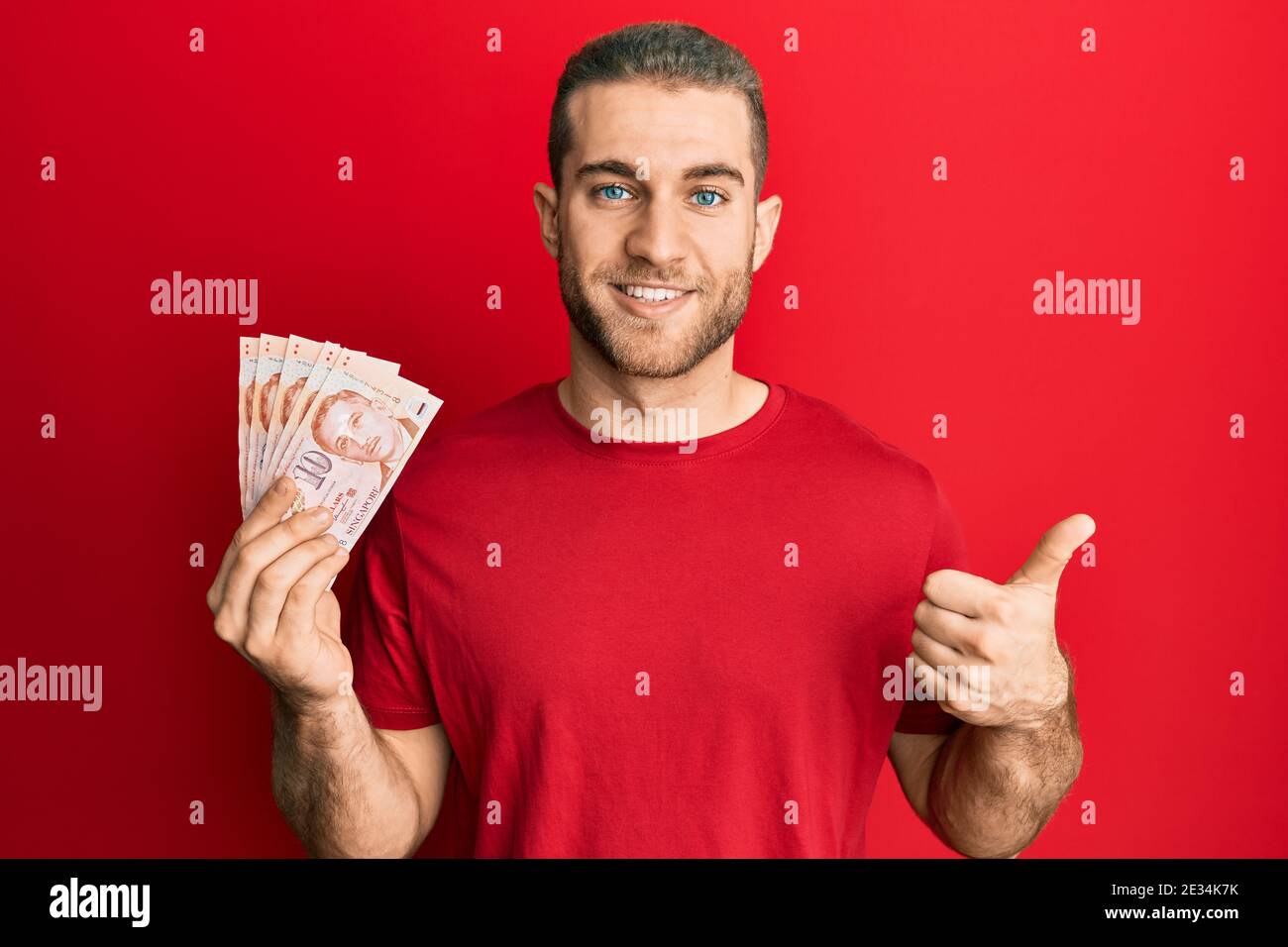 Young caucasian man holding 10 singapore dollars banknotes smiling ...