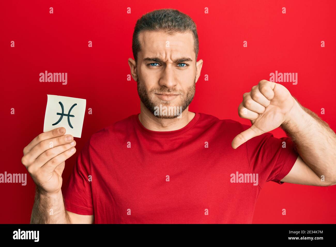 Young caucasian man holding paper with pisces zodiac sign with angry ...