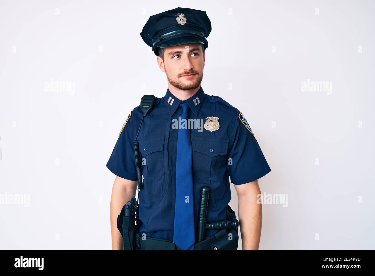 Young caucasian man wearing police uniform smiling looking to the side ...