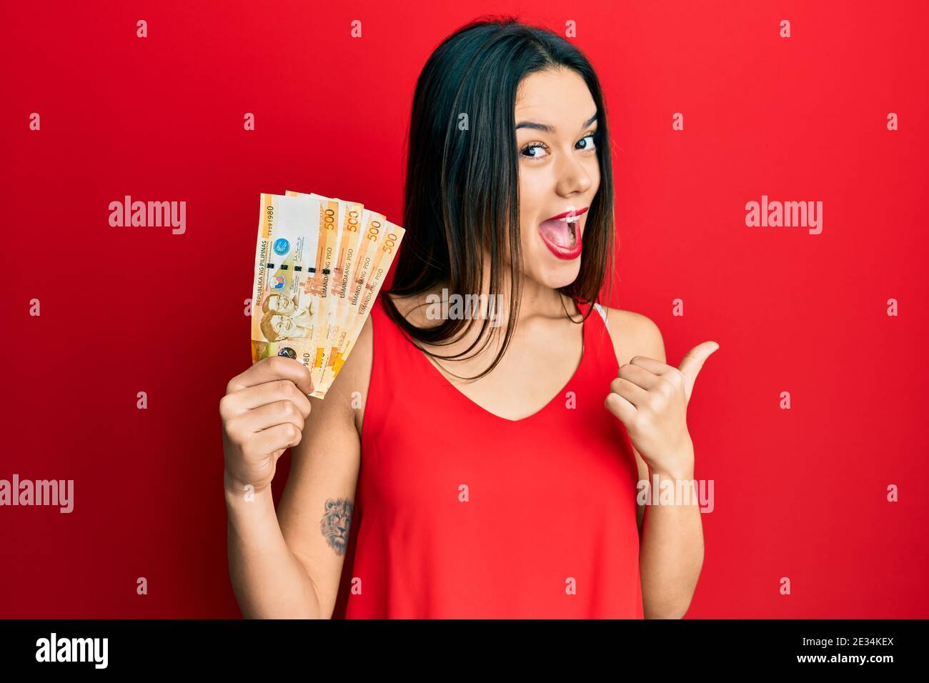 Young hispanic girl holding 500 philippine peso banknotes pointing ...