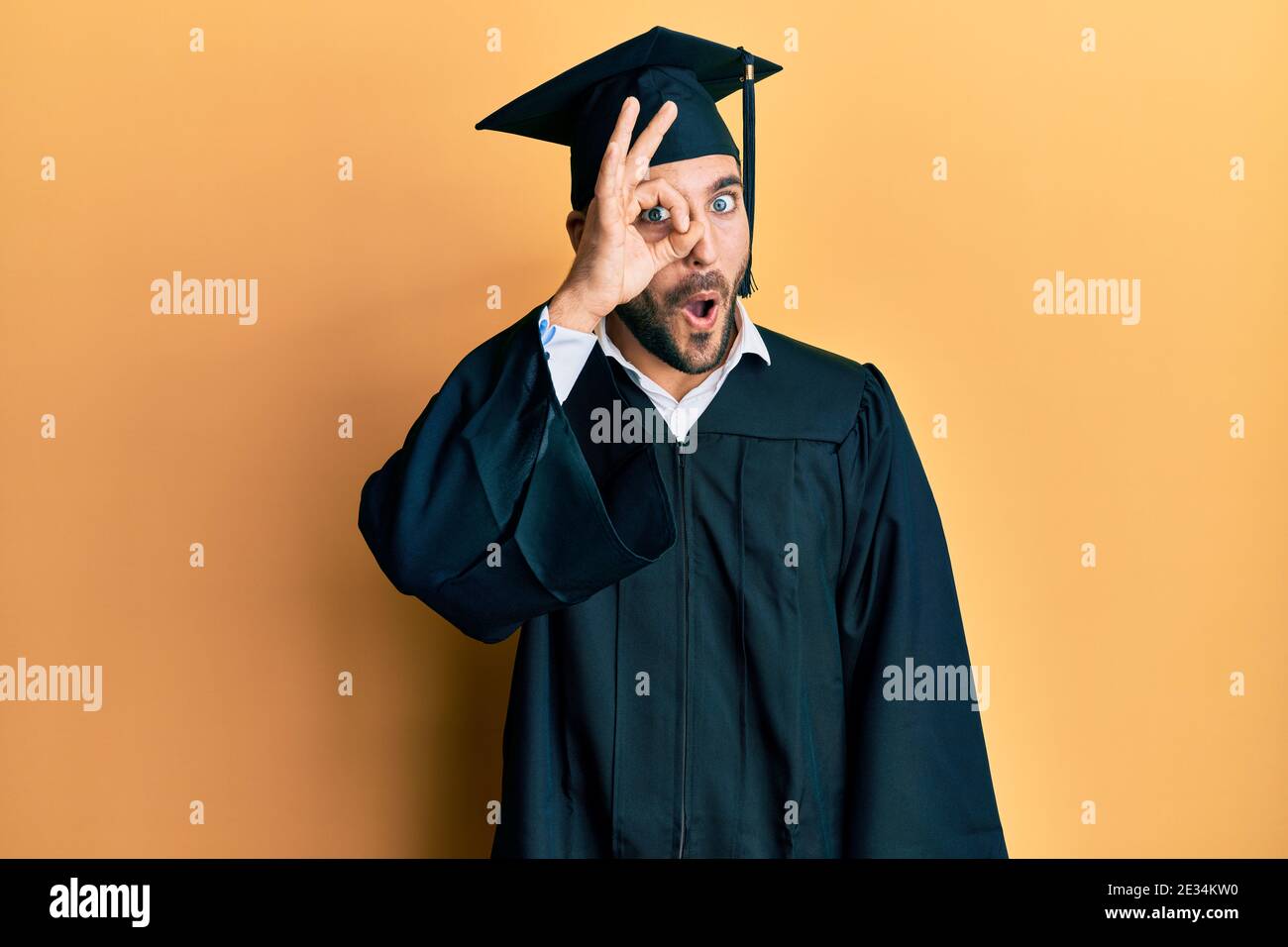 Young hispanic man wearing graduation cap and ceremony robe doing ok ...