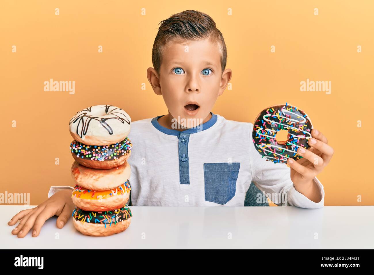 Adorable caucasian kid eating doughnuts for breakfast afraid and ...
