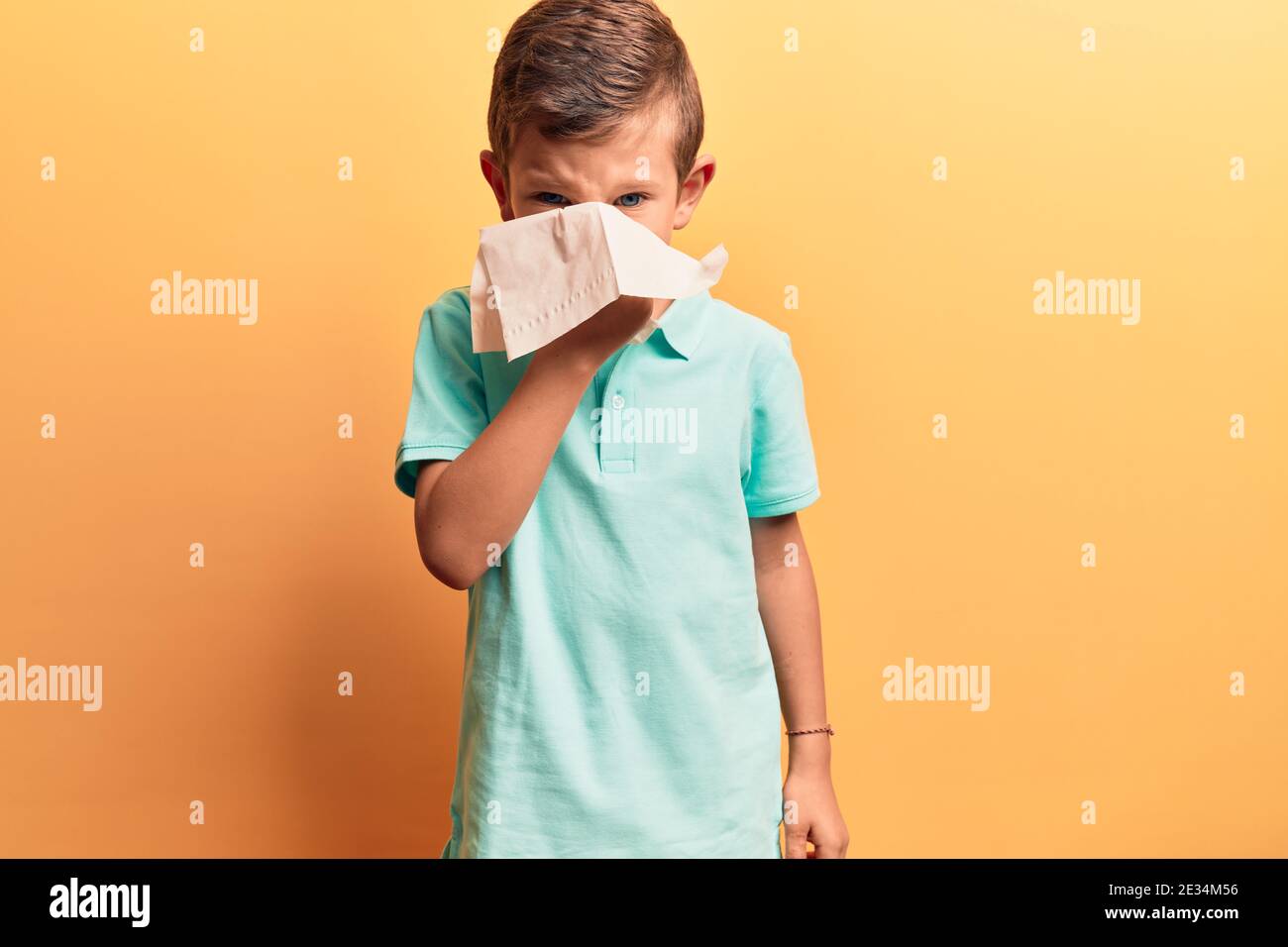 Adorable blonde kid illness using paper handkerchief on nose. Standing ...