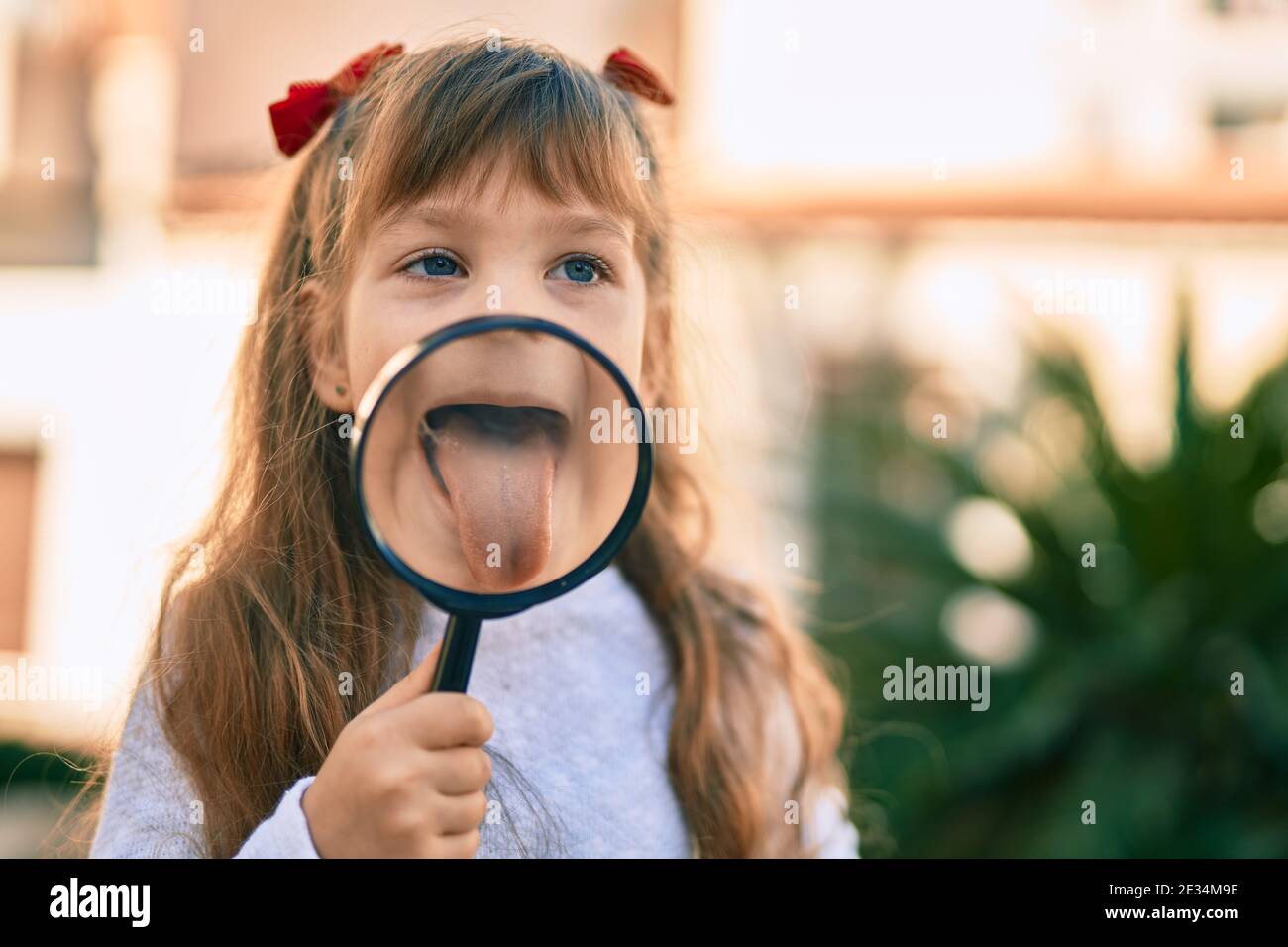 Adorable caucasian child girl with tongue out using loupe at the city ...