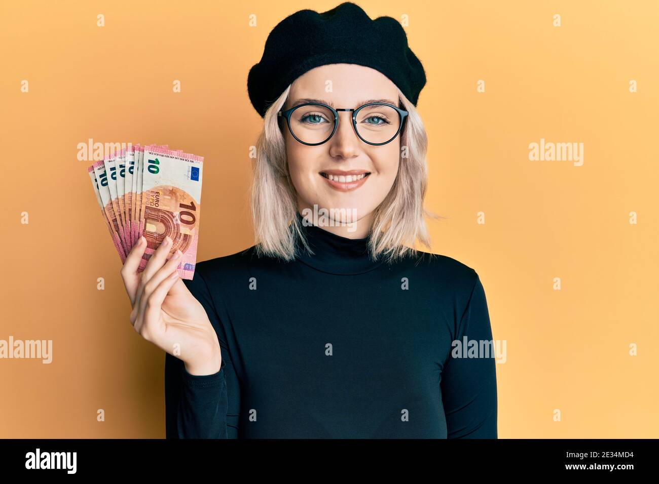 Young blonde girl holding euro banknotes looking positive and happy ...
