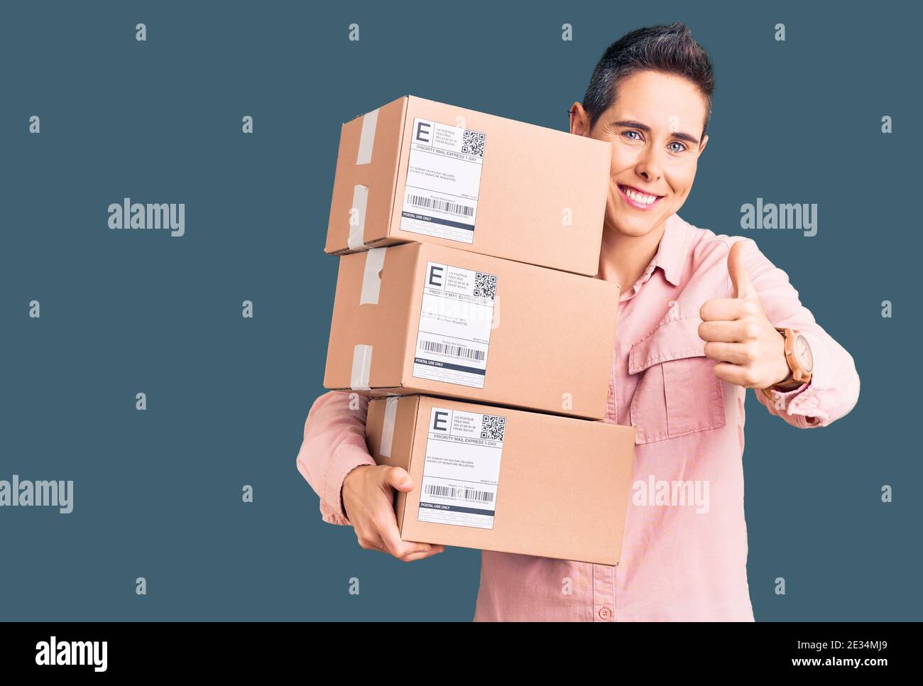 Young woman with short hair holding delivery package smiling happy and ...
