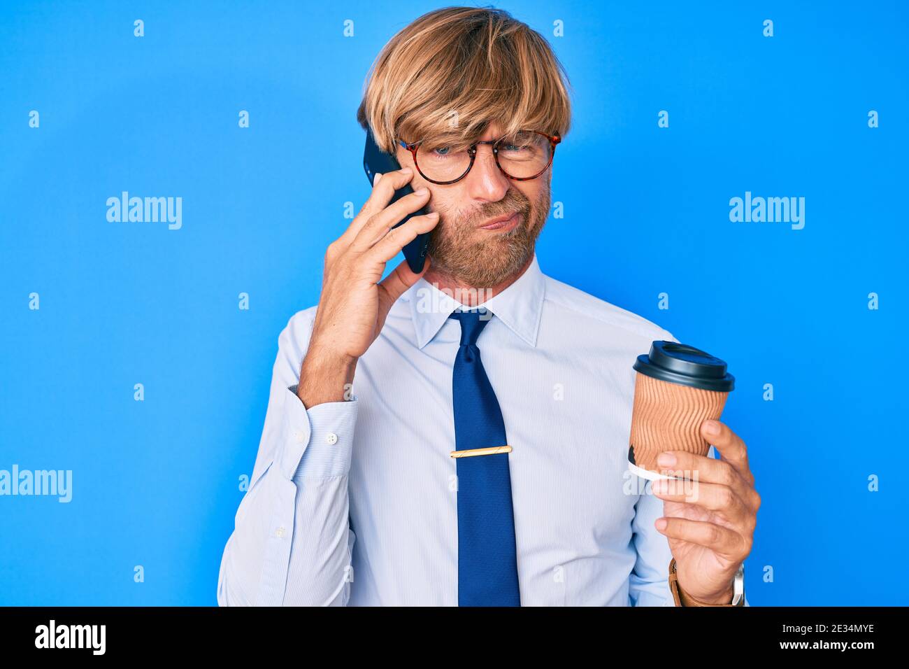 Young blond man talking on the smartphone and drinking a cup of coffee ...