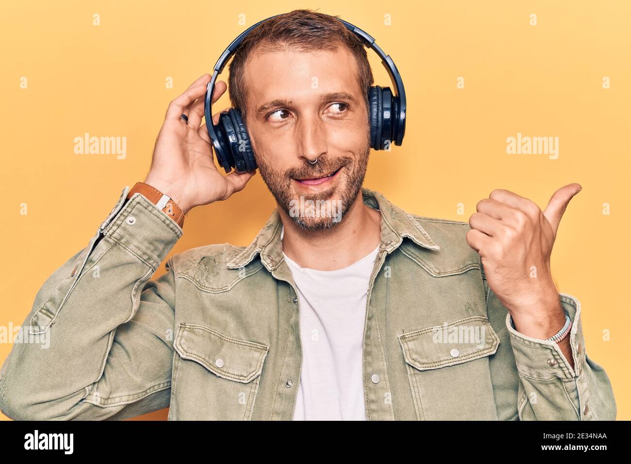 Young handsome man listening to music using headphones pointing thumb ...