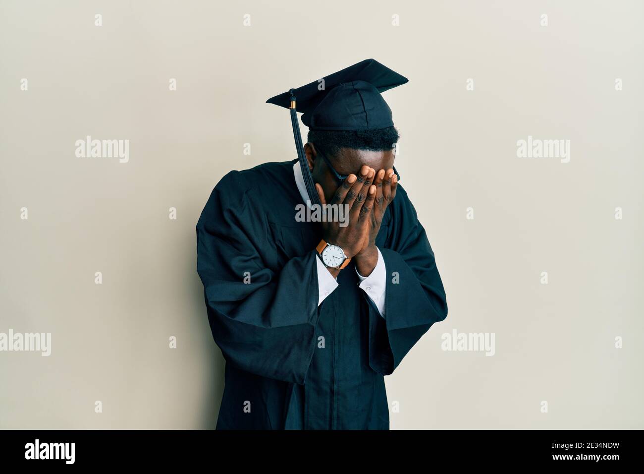 Handsome black man wearing graduation cap and ceremony robe with sad ...