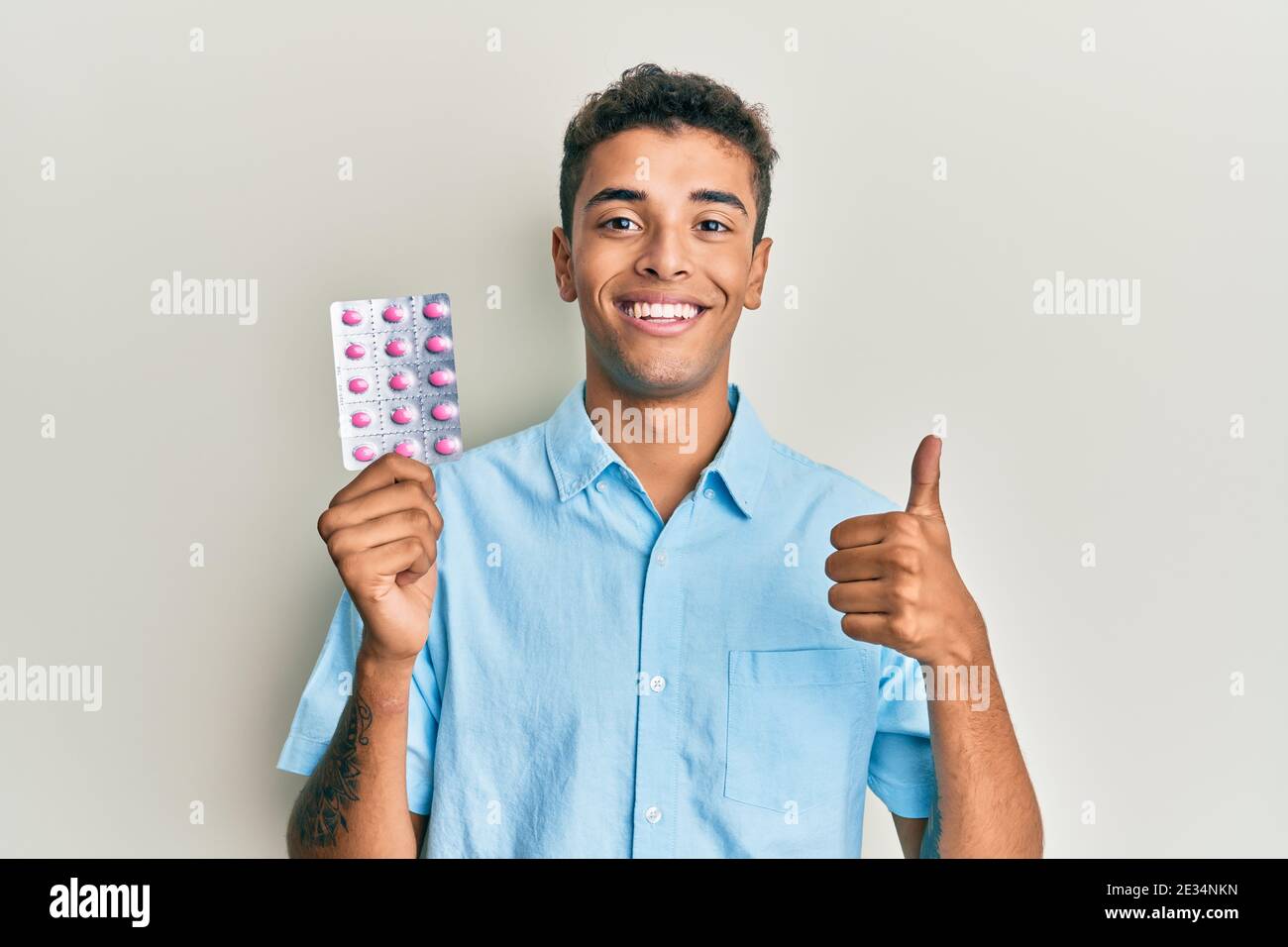 Young handsome african american man holding pills smiling happy and ...
