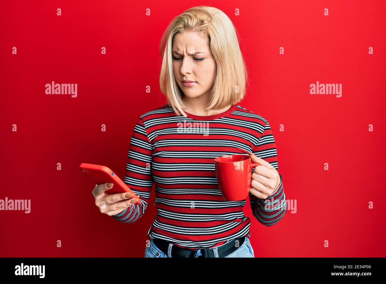 Young blonde woman using smartphone and drinking a cup of coffee ...