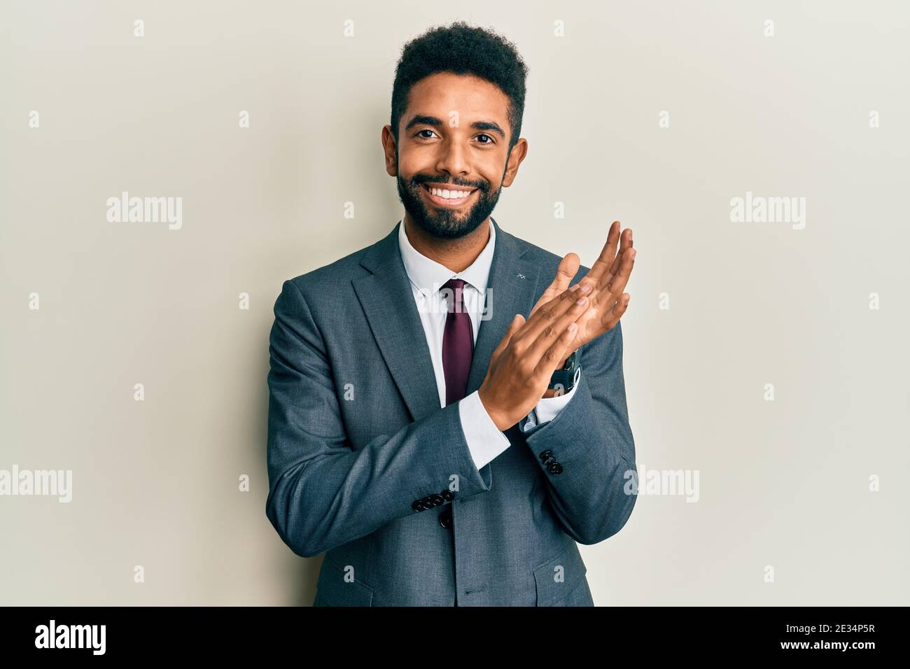 Handsome hispanic man with beard wearing business suit and tie clapping ...