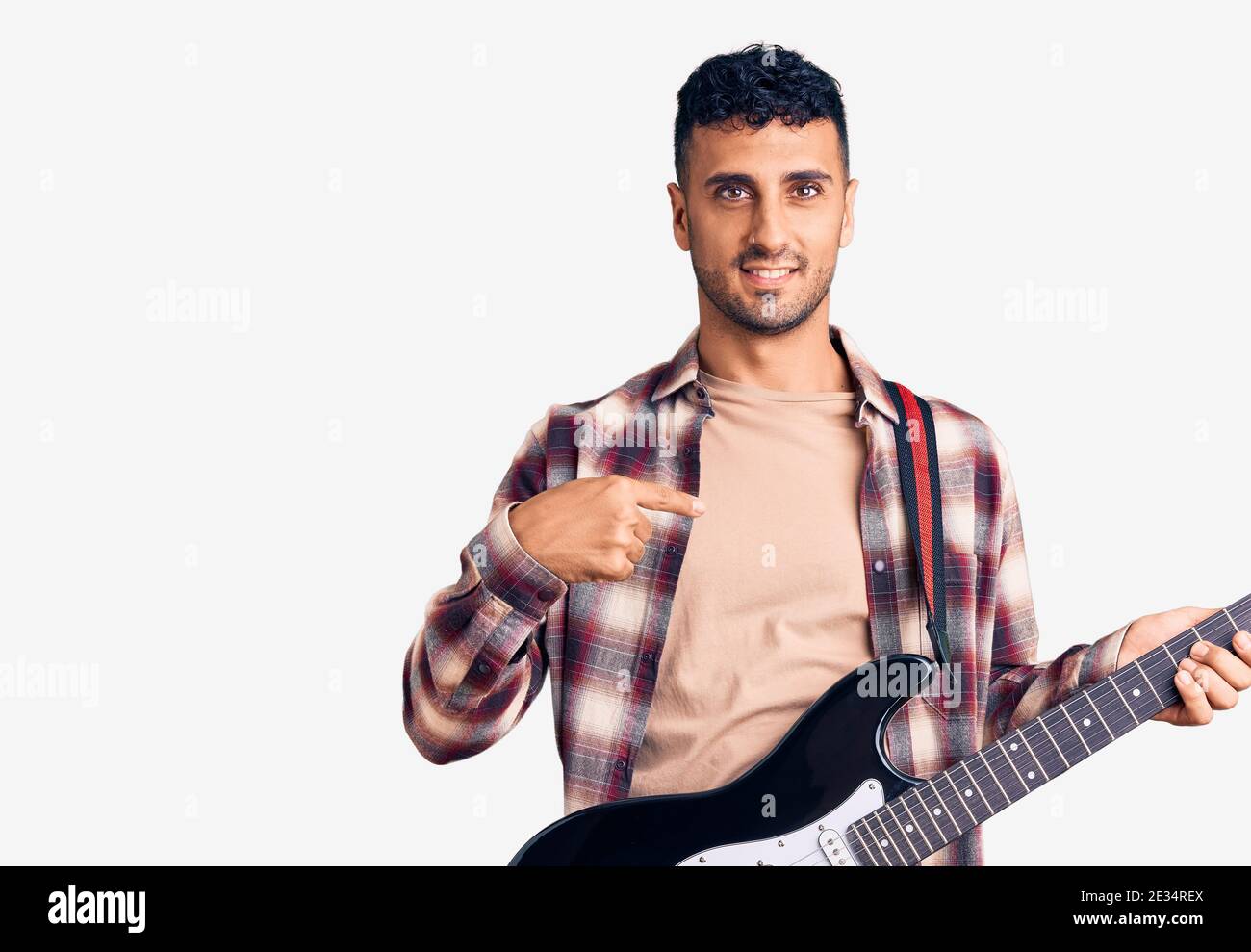 Young hispanic man playing electric guitar pointing finger to one self ...