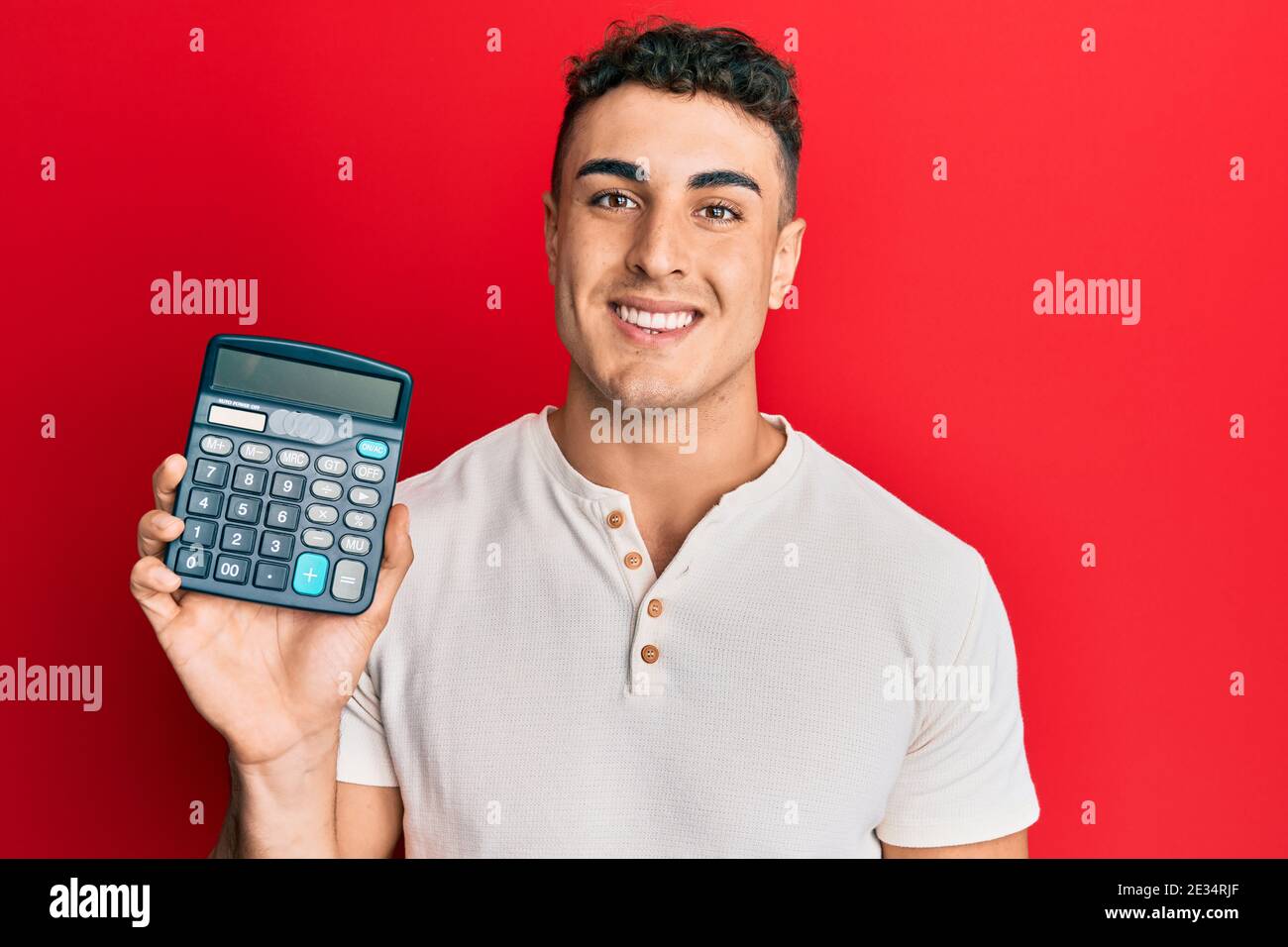 Hispanic young man showing calculator device looking positive and happy ...