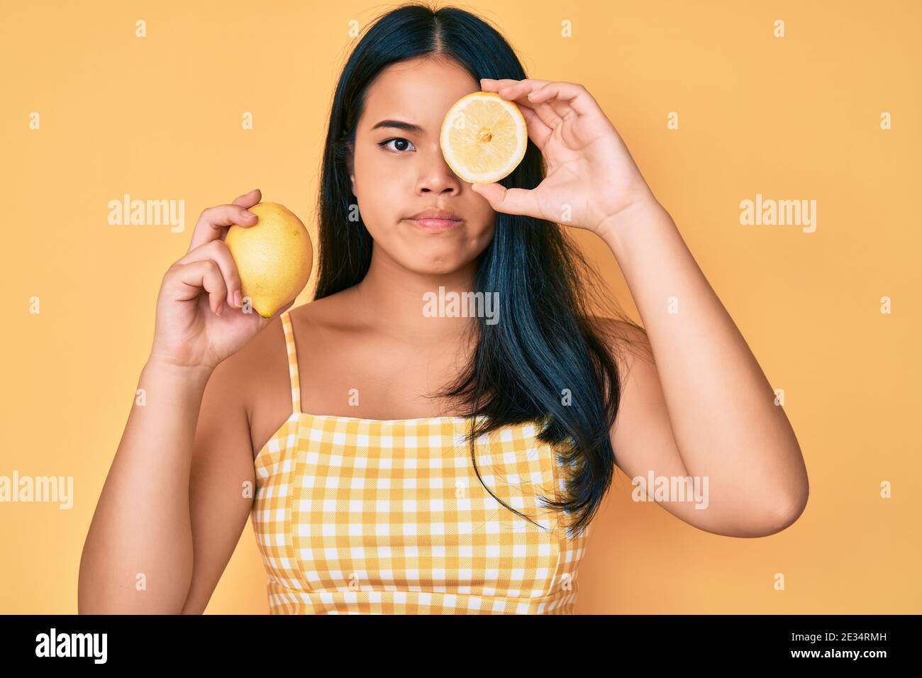 Young beautiful asian girl holding lemon skeptic and nervous, frowning upset because of problem ...
