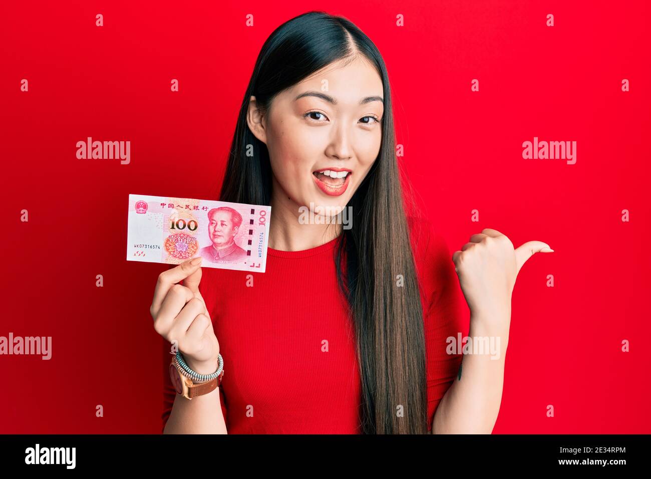 Young chinese woman holding 100 yuan chinese banknote pointing thumb up ...