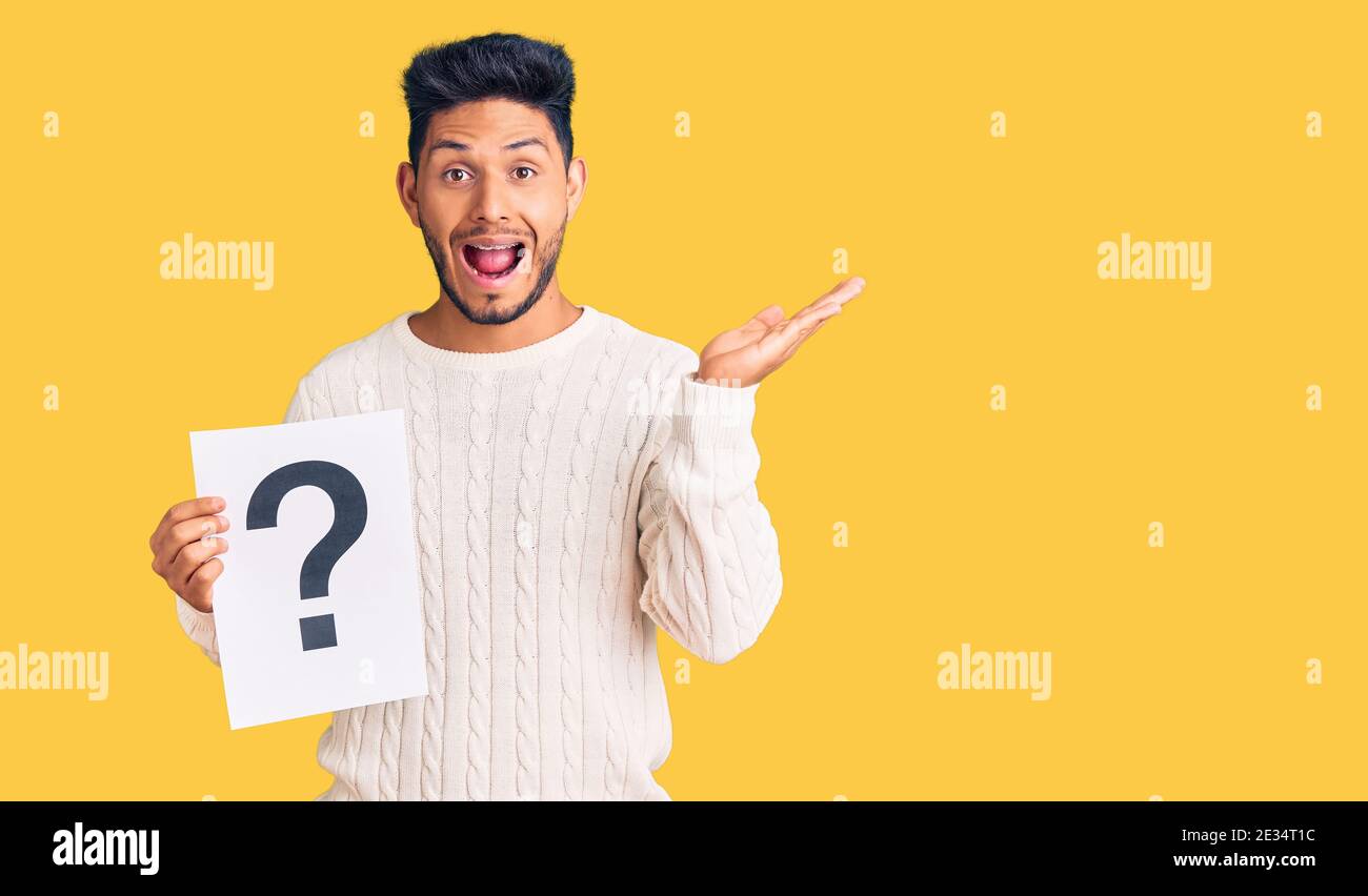 Handsome latin american young man holding question mark celebrating ...