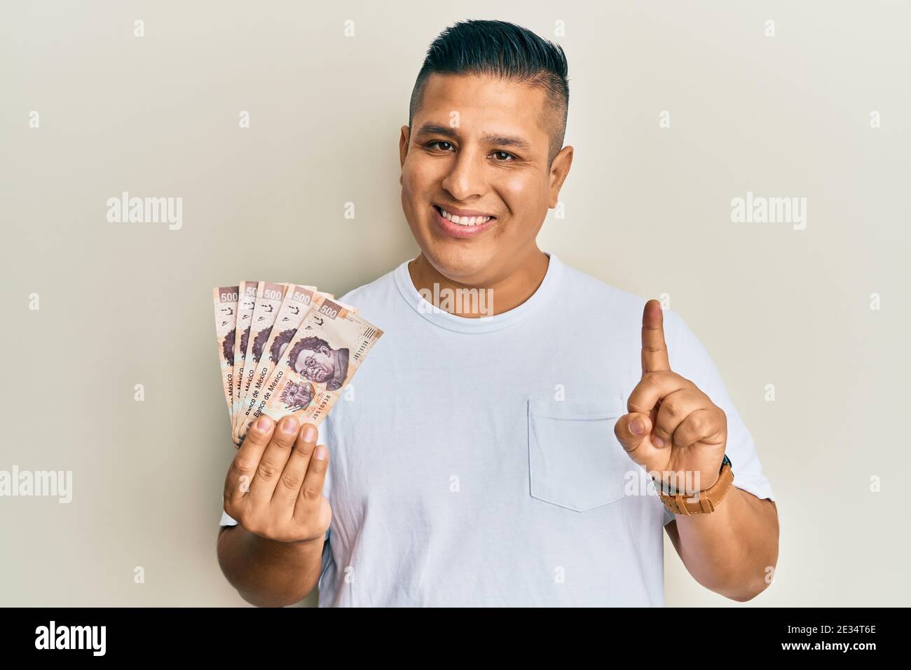 Young latin man holding 500 mexican pesos banknotes smiling with an ...