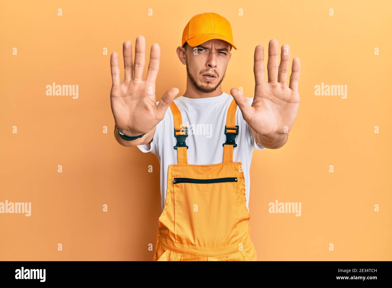 Hispanic young man wearing handyman uniform doing stop gesture with ...