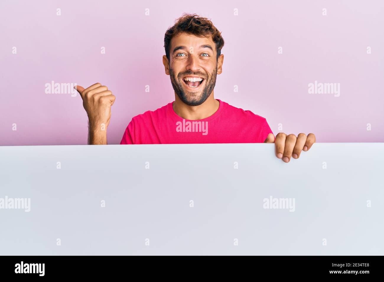 Handsome man with beard holding blank empty banner pointing thumb up to ...