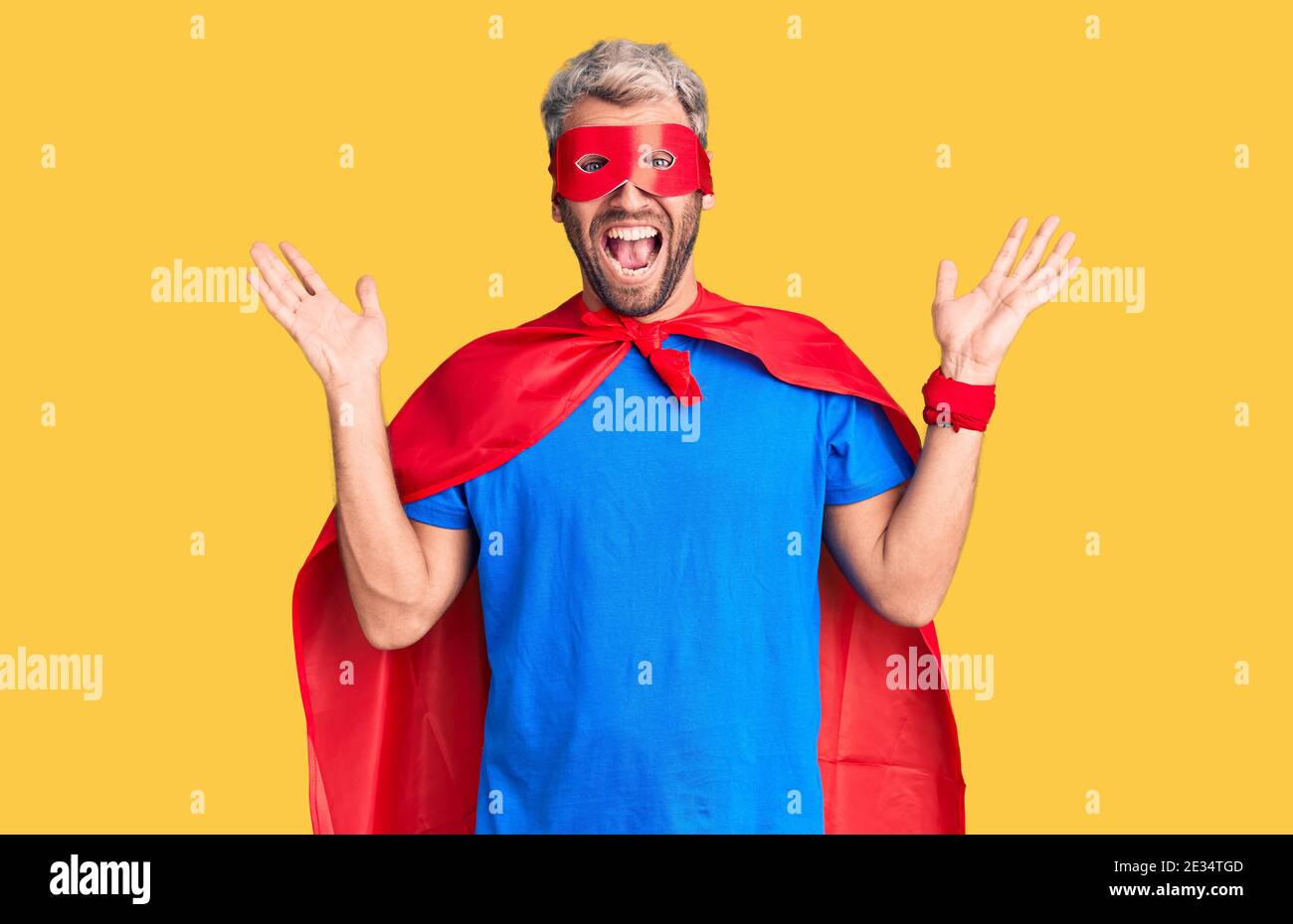 Young blond man wearing super hero custome celebrating crazy and amazed ...