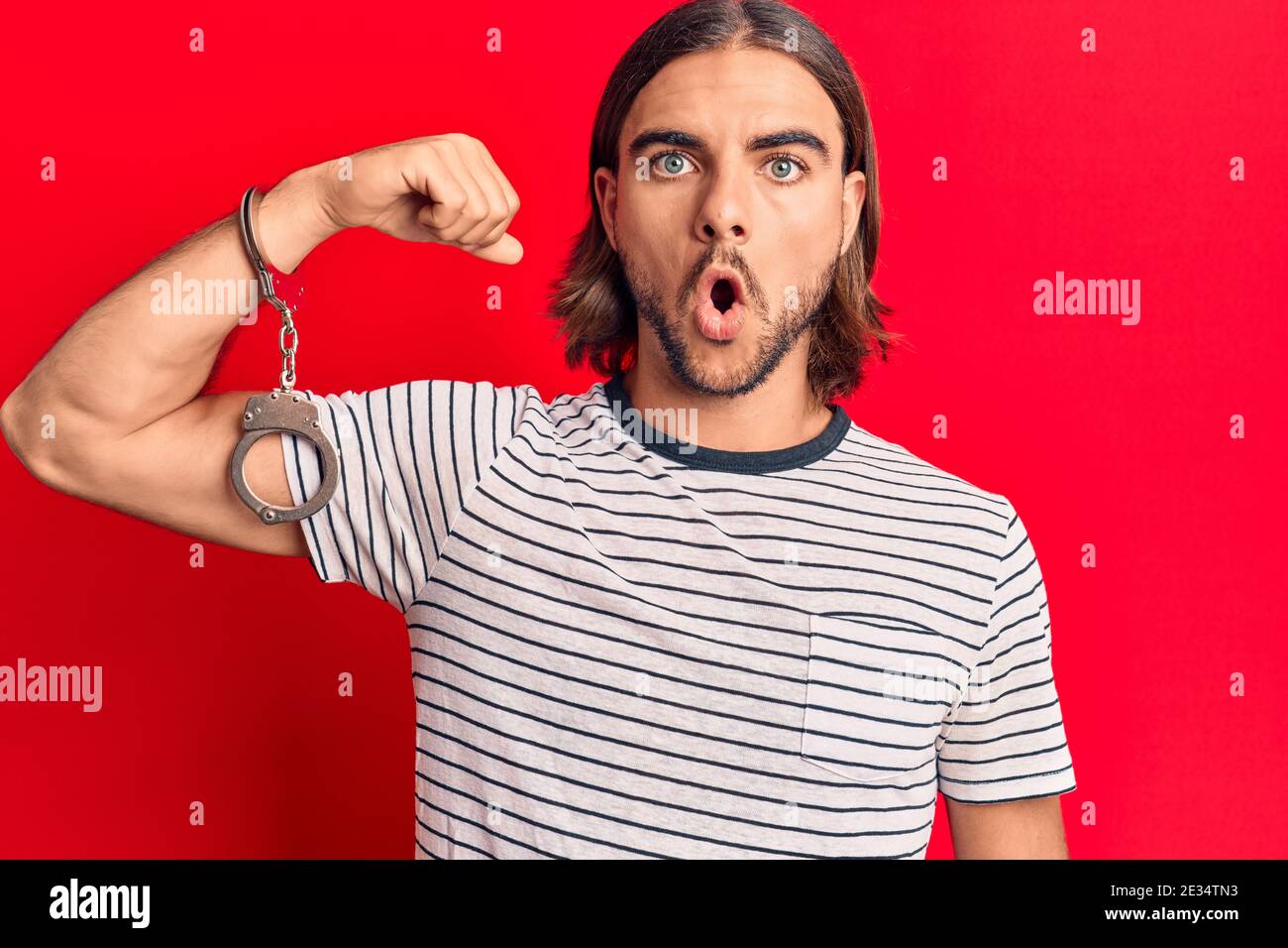Young handsome man wearing prisoner handcuffs scared and amazed with ...
